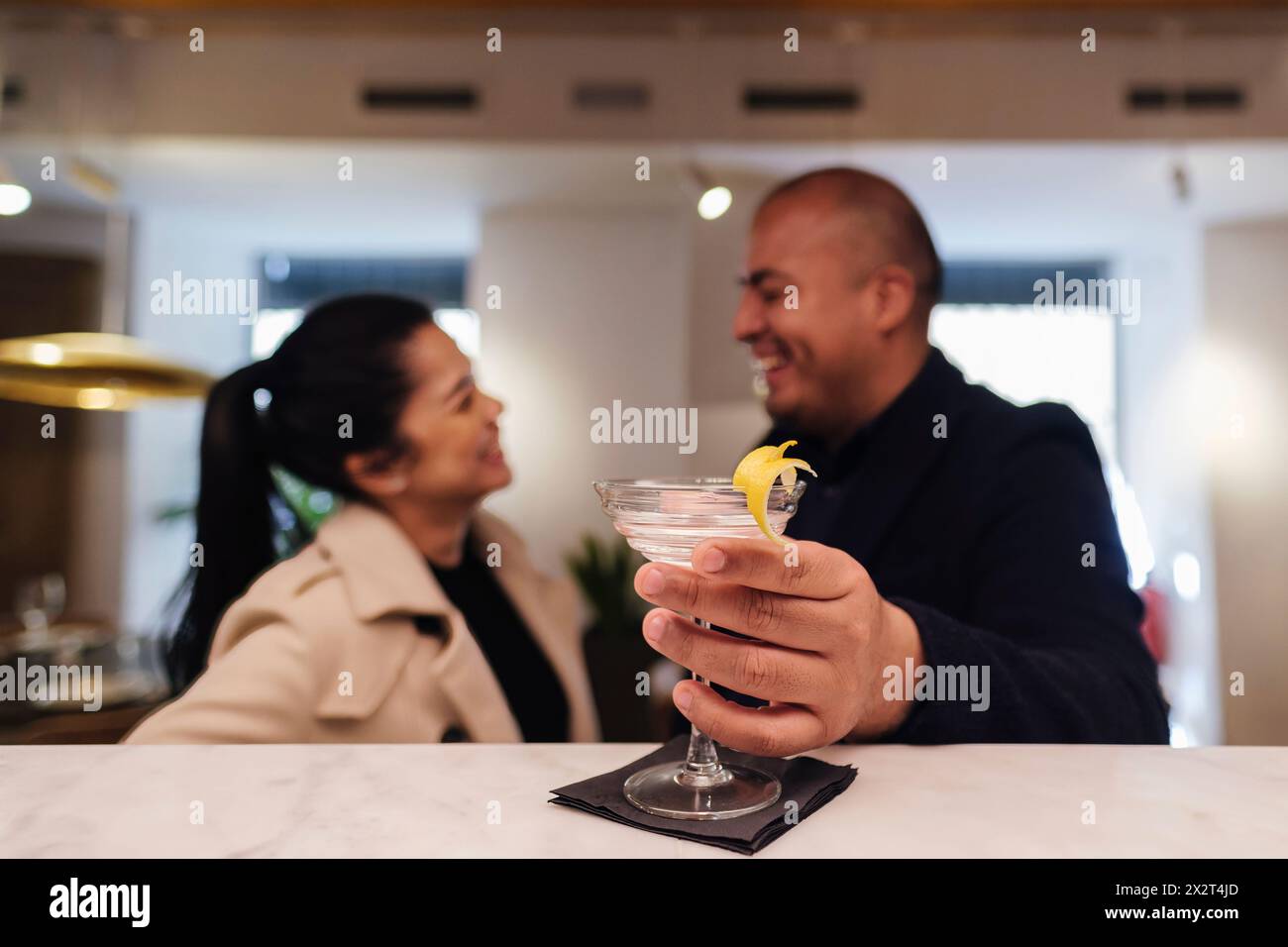 Couple talking to each other with cocktail at illuminated bar counter ...