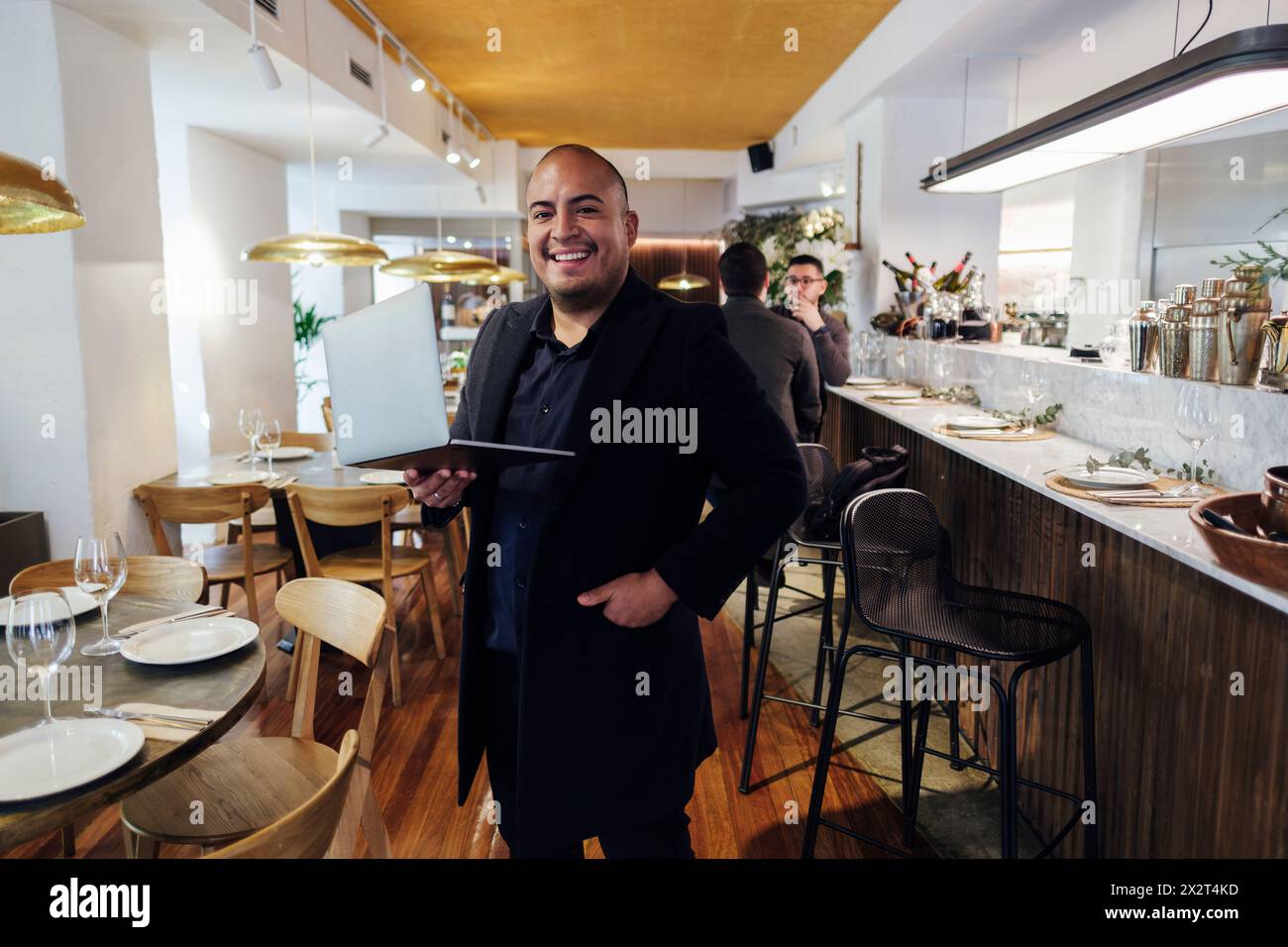 Smiling customer standing with laptop at illuminated restaurant Stock ...