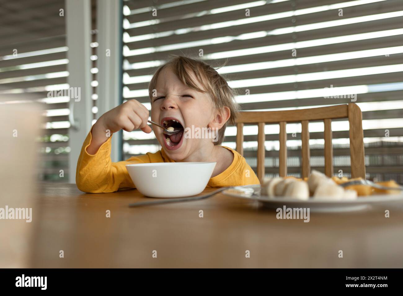 Hungry boy eating breakfast with spoon at home Stock Photo - Alamy