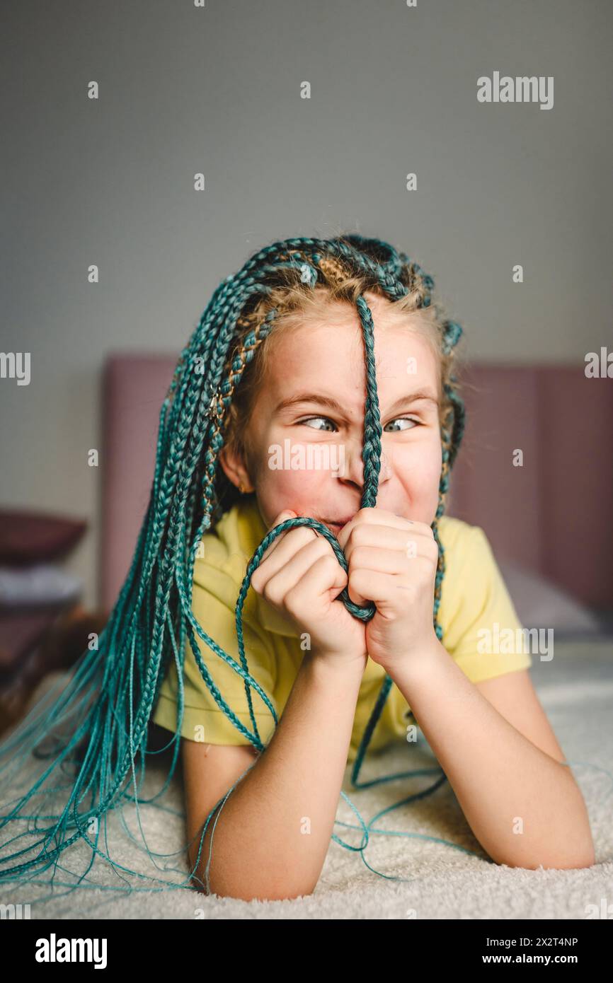 Girl playing with turquoise dyed braided hair lying on bed at home ...
