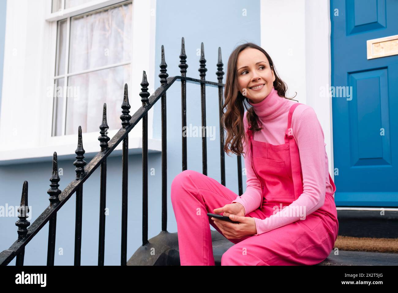 Happy beautiful woman wearing pink bib overalls with smart phone ...