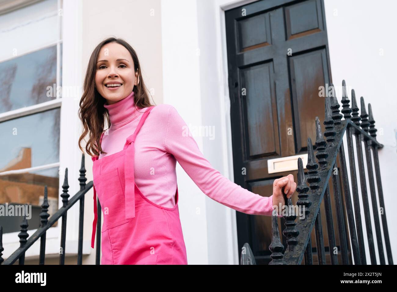 Happy woman wearing pink bib overalls in front of blue door Stock Photo ...