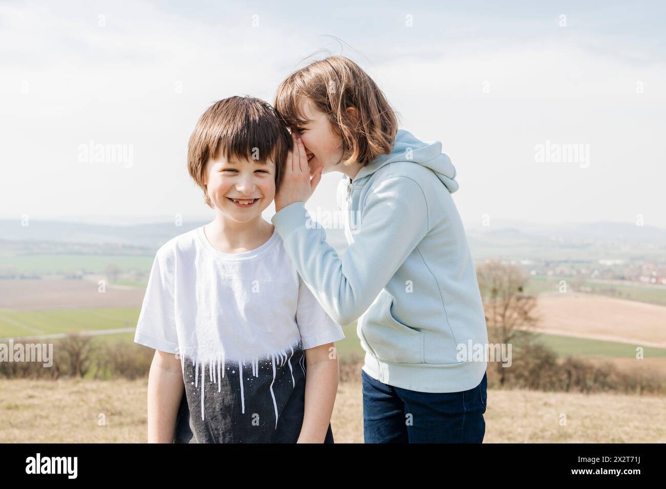 Smiling girl whispering in brother's ear standing on hill Stock Photo ...