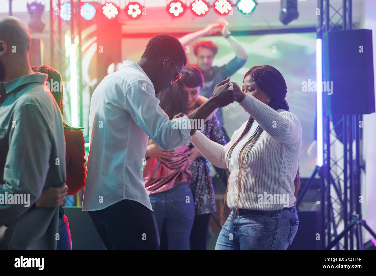 Young man and woman friends holding hands while dancing at nightclub ...
