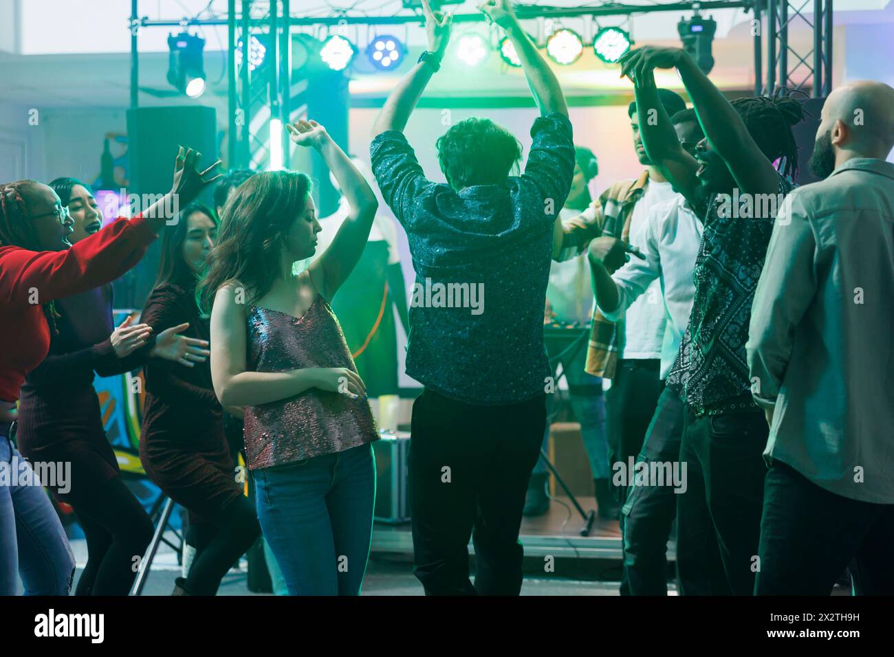 Active people dancing and raising hands while partying in nightclub. Young men and women moving ...
