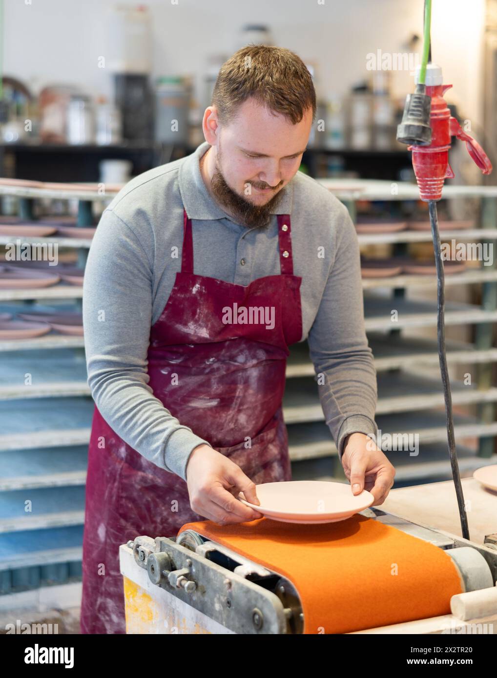 Bearded ceramicist smoothing pottery plate using belt sander Stock ...