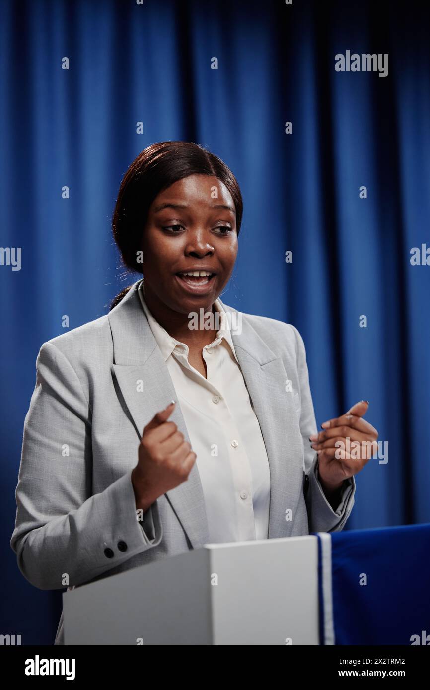 Young female politician in grey suit standing by platform in conference ...
