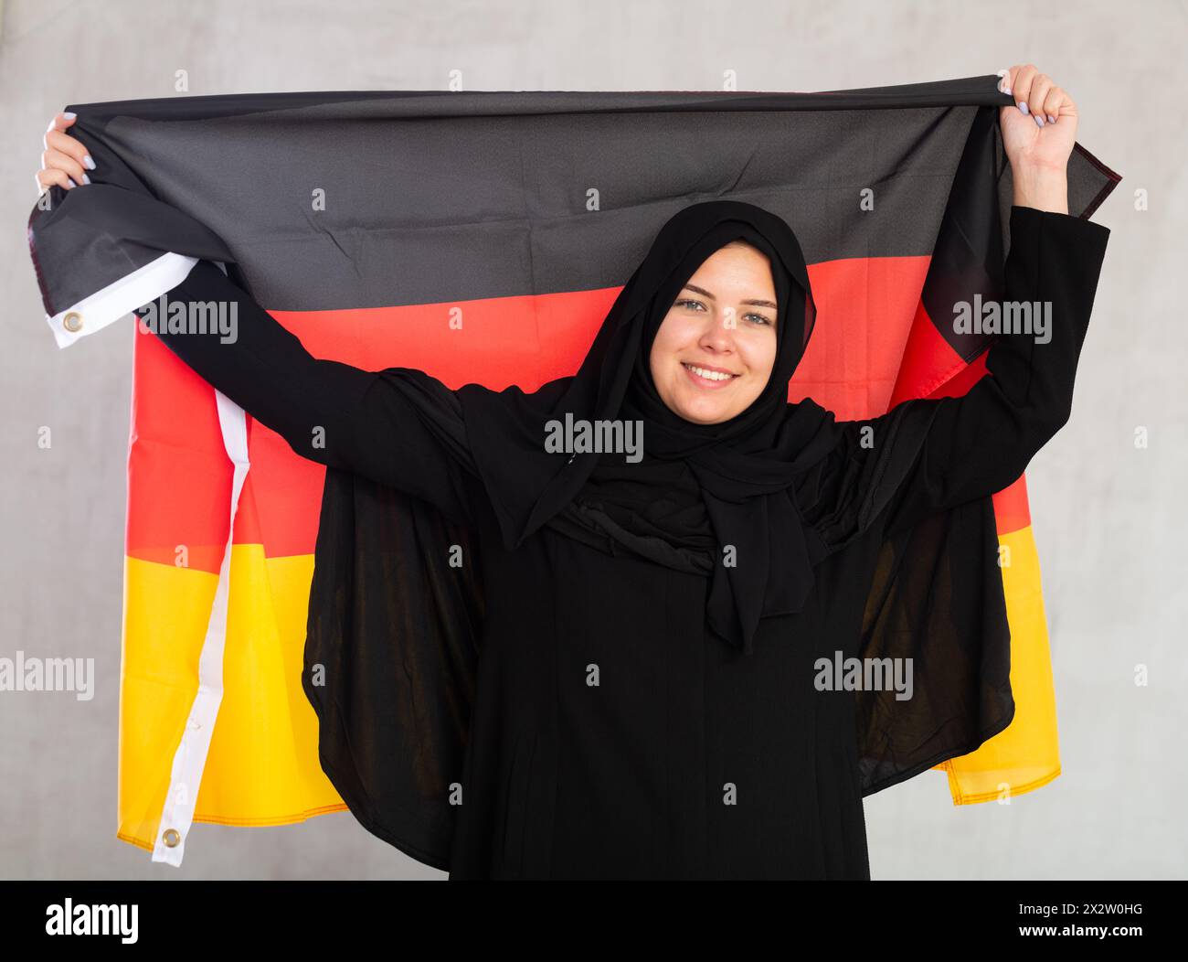 smiling Muslim woman in traditional black hijab holds flag of Germany ...