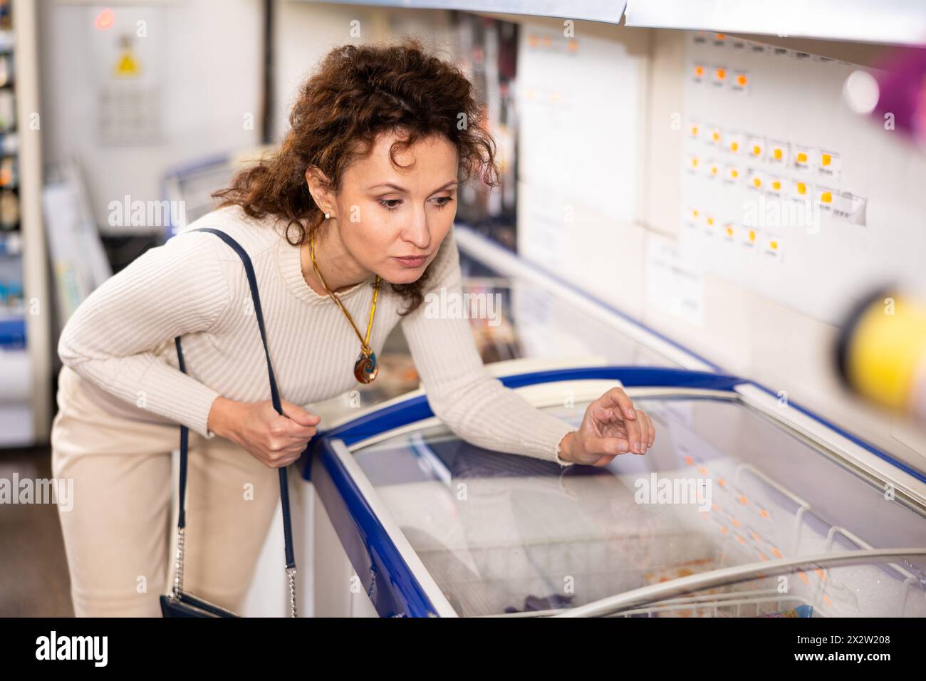 woman looks and chooses frozen food in refrigerator in grocery ...