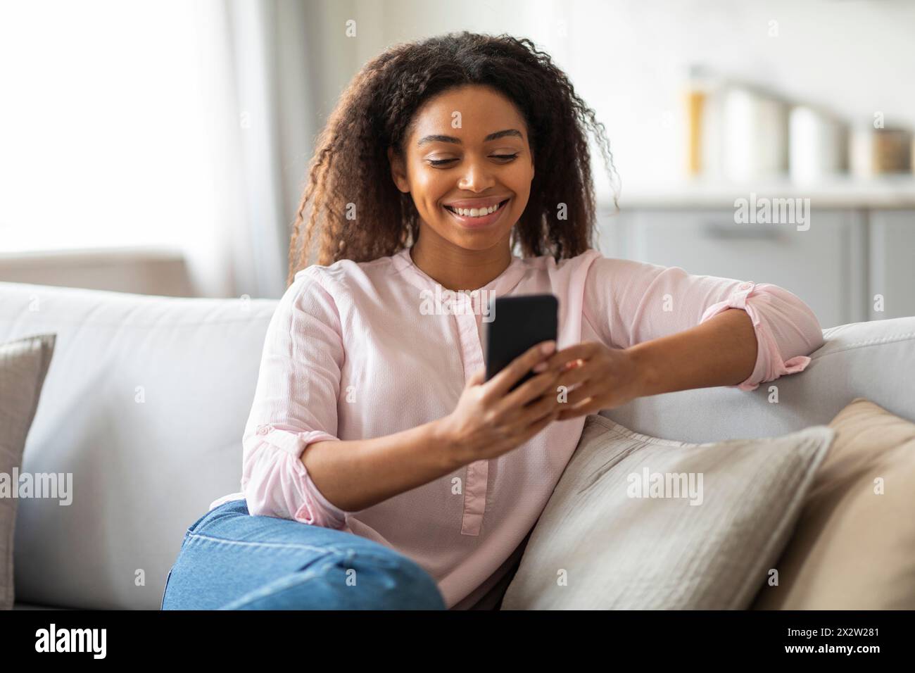 Black woman texting on smartphone in home setting Stock Photo - Alamy