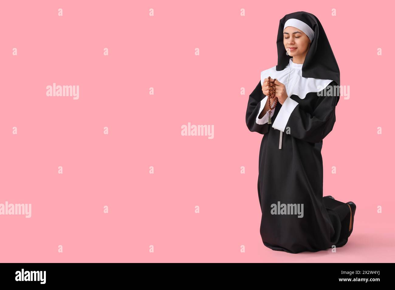 Young nun with beads praying on pink background Stock Photo - Alamy