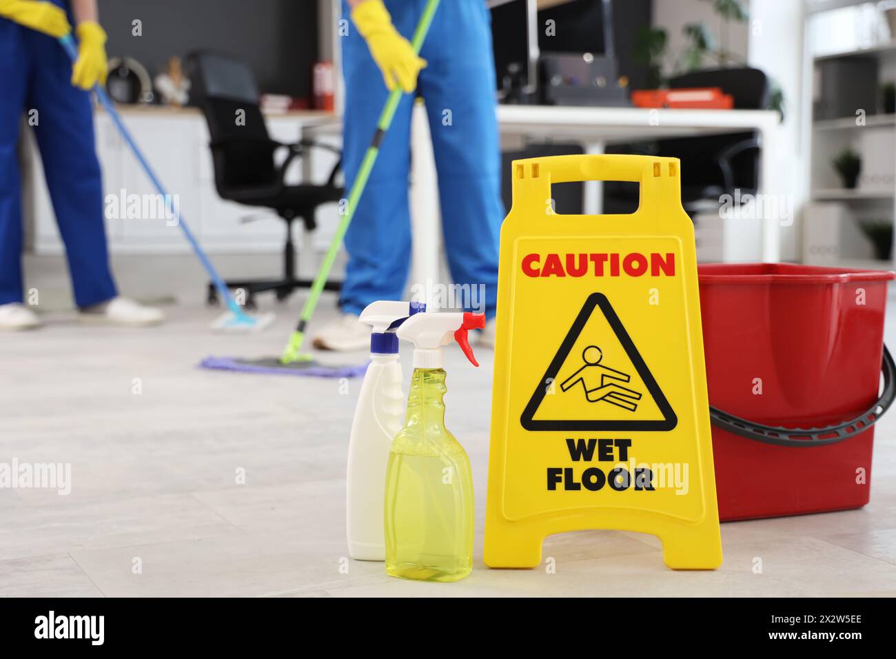 Caution sign with bottles of detergent and bucket on floor in office ...