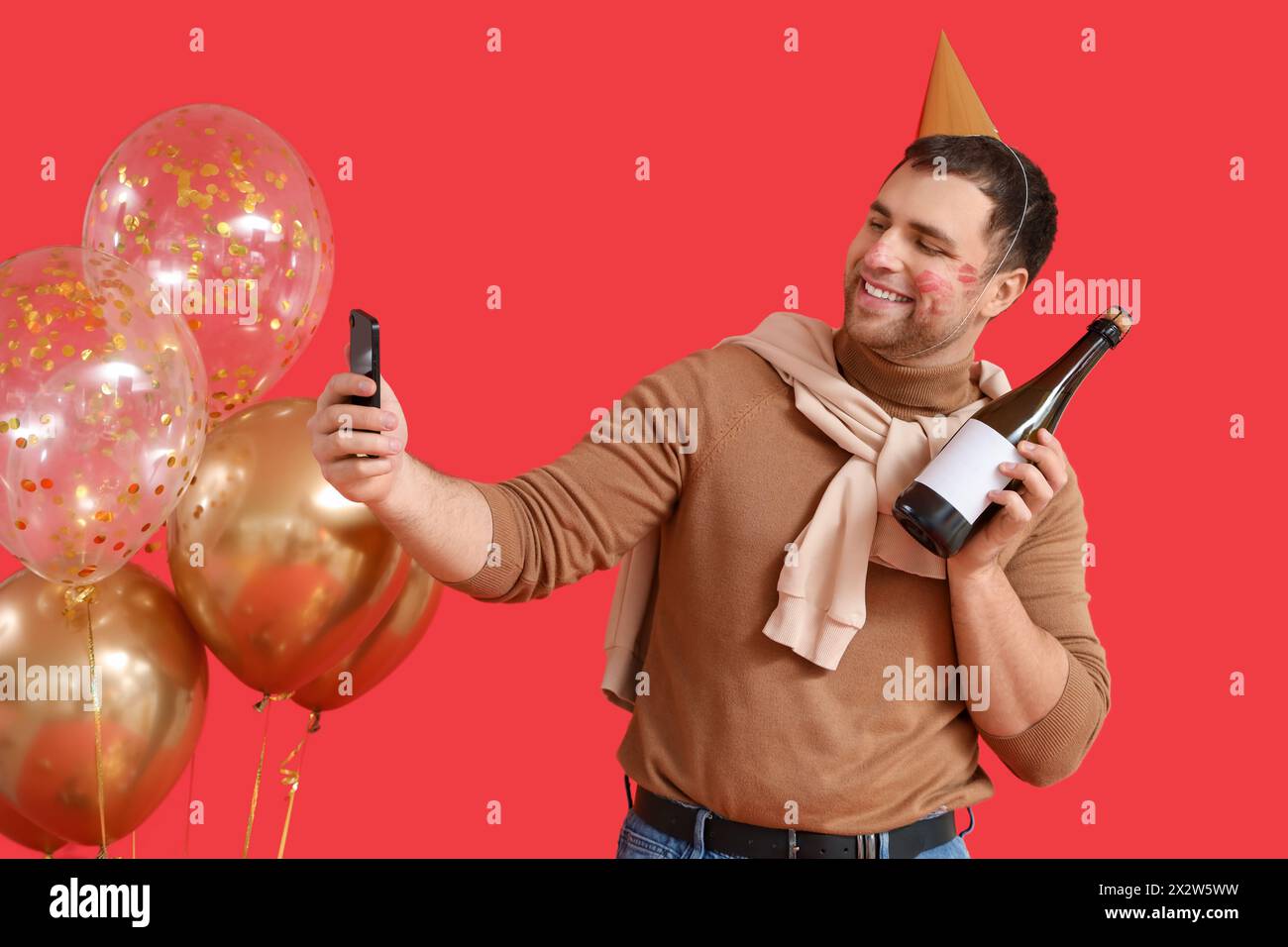 Drunk young man with lipstick kiss marks and champagne taking selfie ...