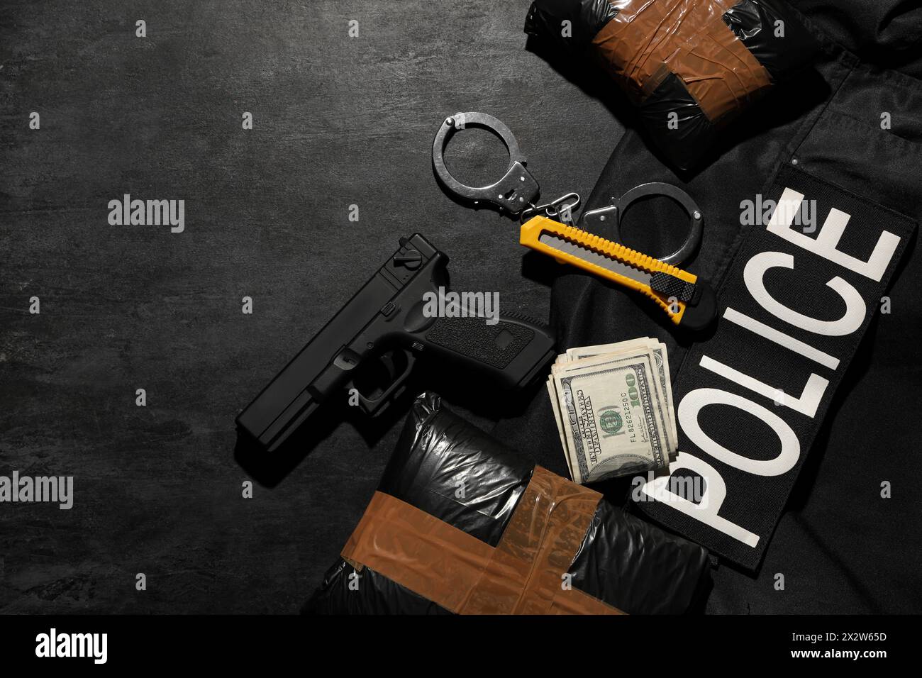 Drug packages with gun, money and police uniform on dark background ...