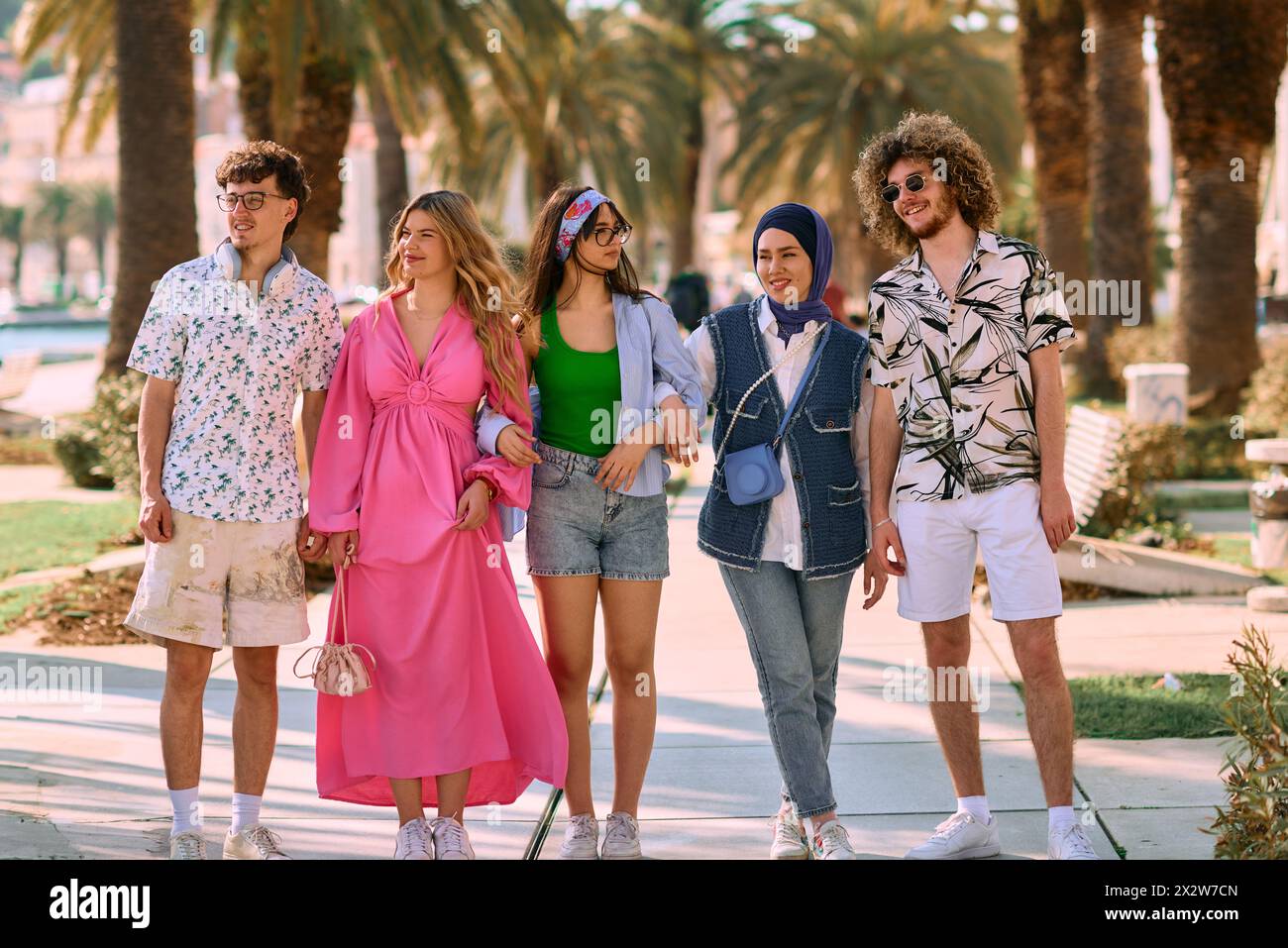 A diverse group of tourists, dressed in summer attire, strolls through ...
