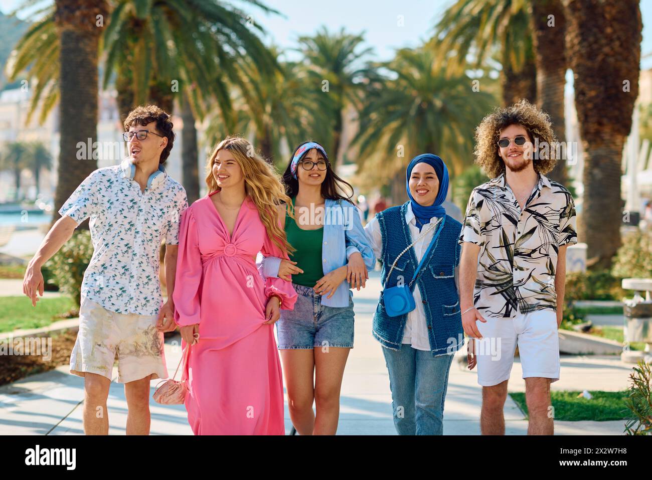 A diverse group of tourists, dressed in summer attire, strolls through ...