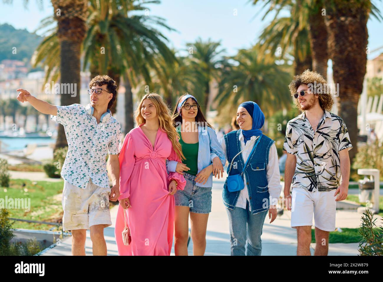 A diverse group of tourists, dressed in summer attire, strolls through ...