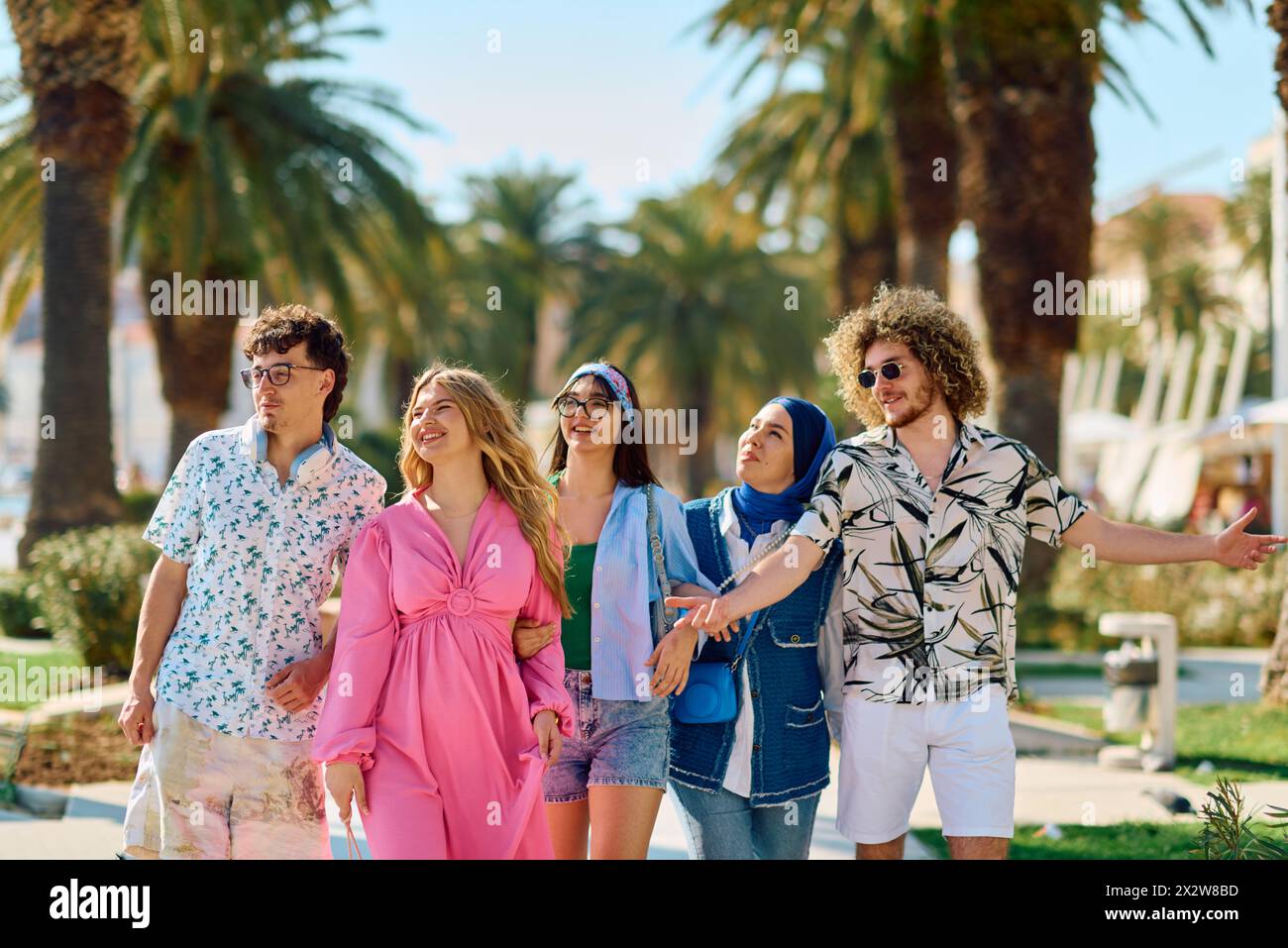 A diverse group of tourists, dressed in summer attire, strolls through ...