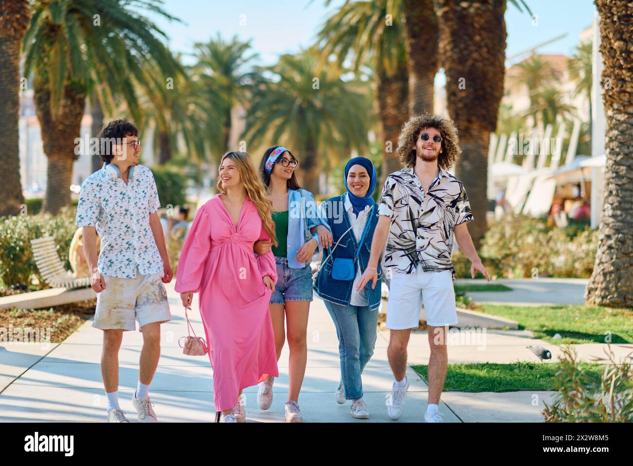 A diverse group of tourists, dressed in summer attire, strolls through ...