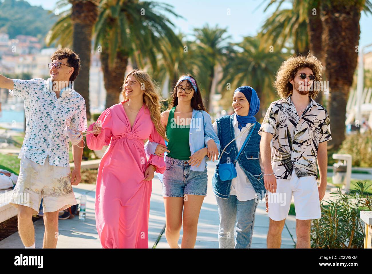 A diverse group of tourists, dressed in summer attire, strolls through ...
