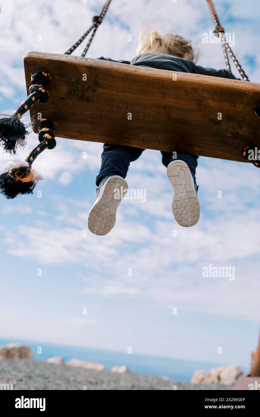 Little girl swings on a rope swing on the seashore against the sky. Bottom view Stock Photo - Alamy