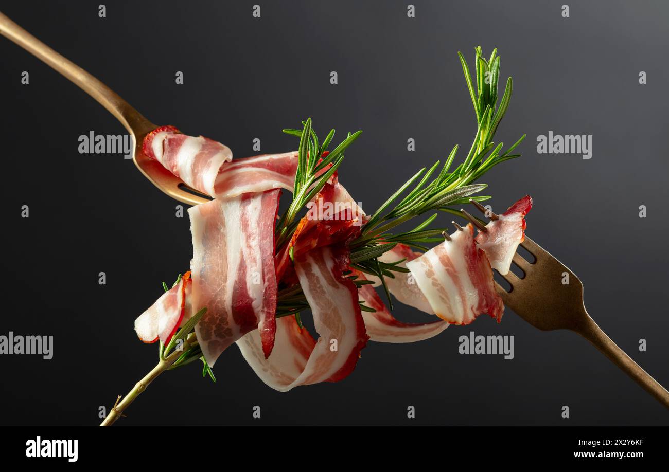 Dry-cured pork belly bacon with rosemary on a black background. Sliced ...