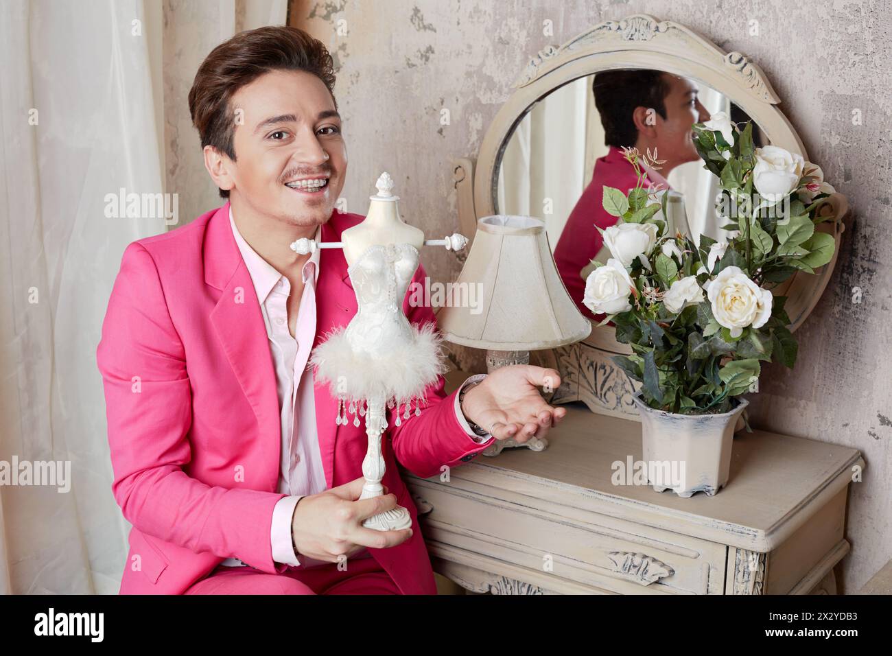 Actor in pink suit sits holding stylized statuette at table with mirror ...