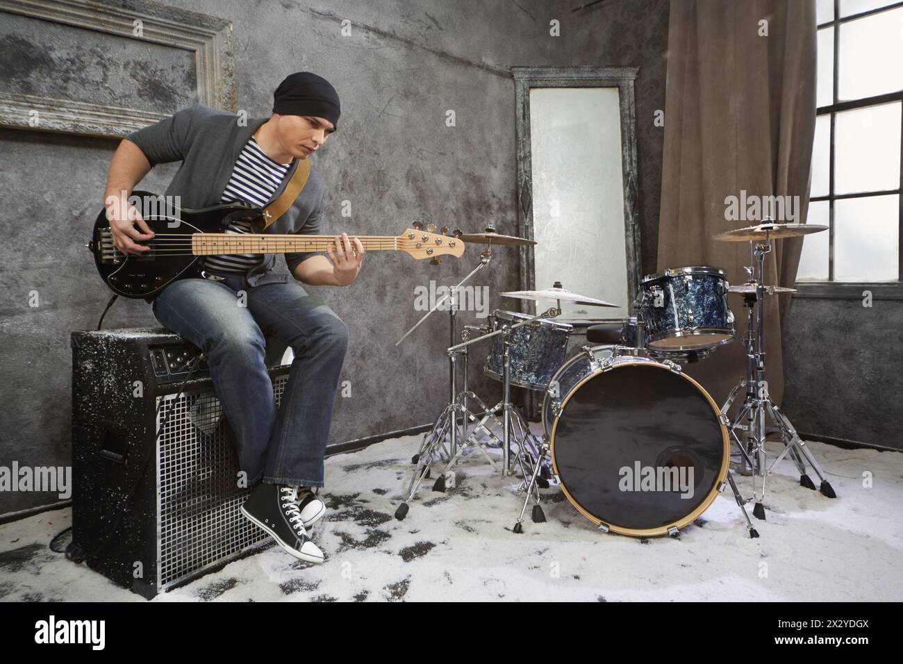 Young musician plays bass electric guitar sitting on amplifier in room ...