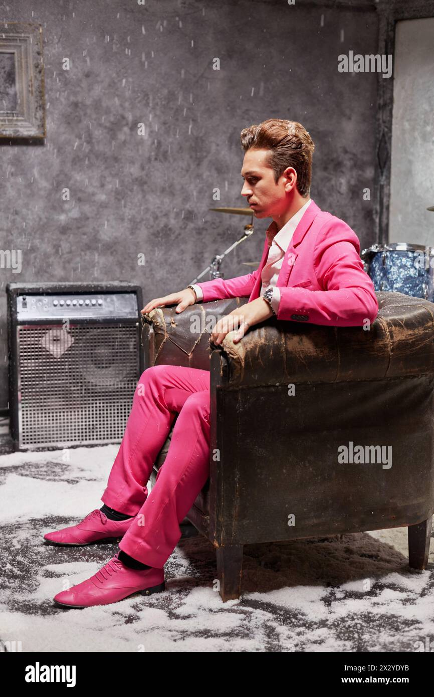 Profile portrait of young man in pink suit who sits motionlessly in old ...