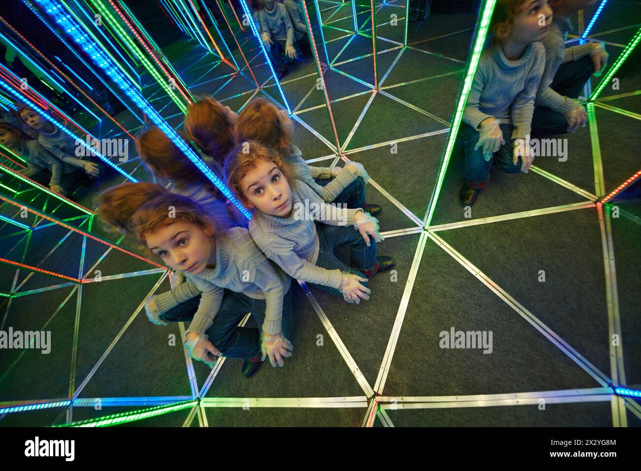 Little girl sits at crossing in mirror labyrinth illuminated with color ...