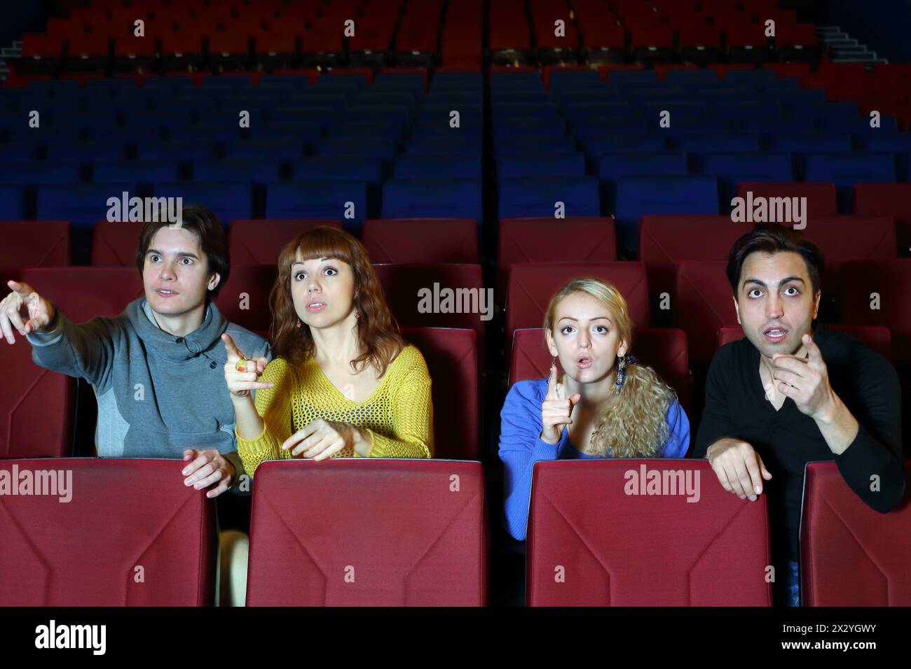 Four young friends amaze and point finger at screen in cinema theater ...
