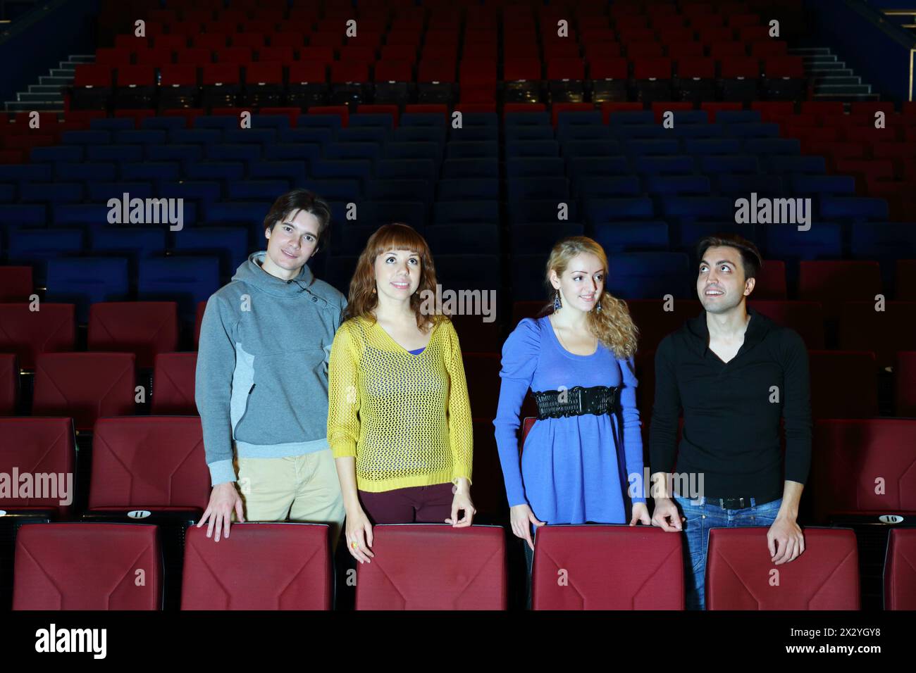 Four happy young friends stand in cinema theater and look in different ...