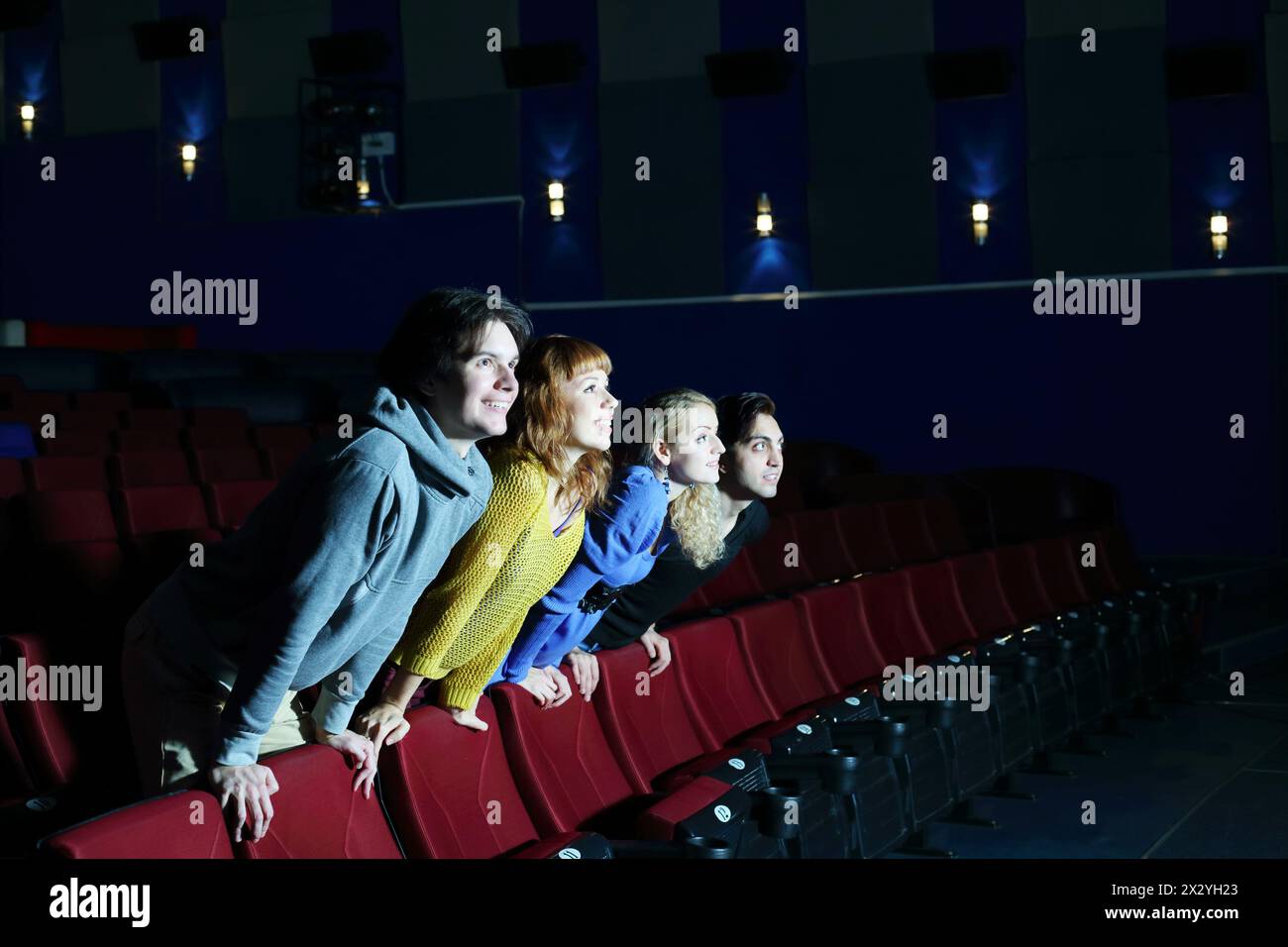 Four happy friends leaned over backs of chairs and look at screen in ...