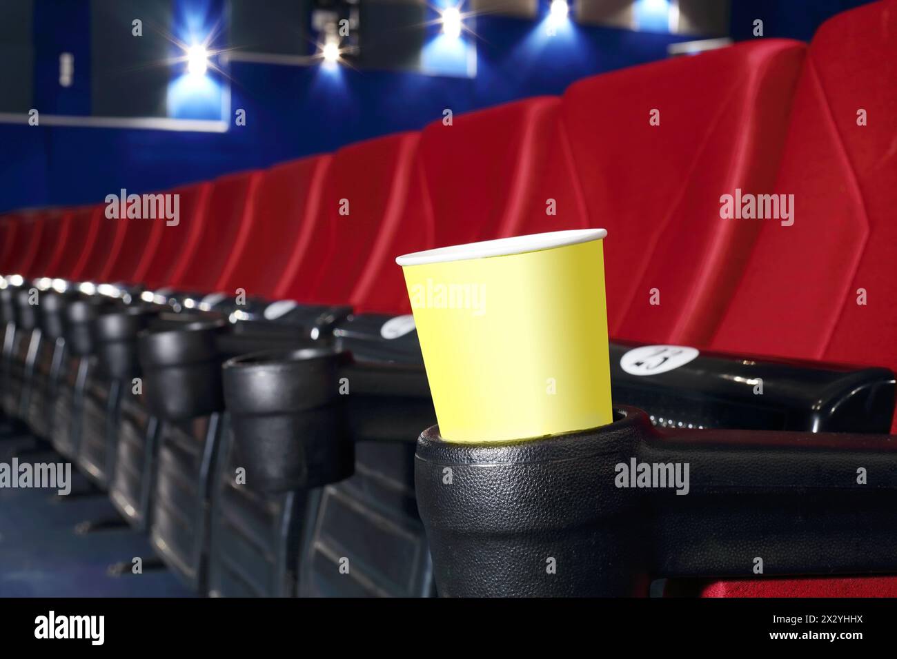 Yellow cup for popcorn is stand at red seat in auditorium in cinema ...