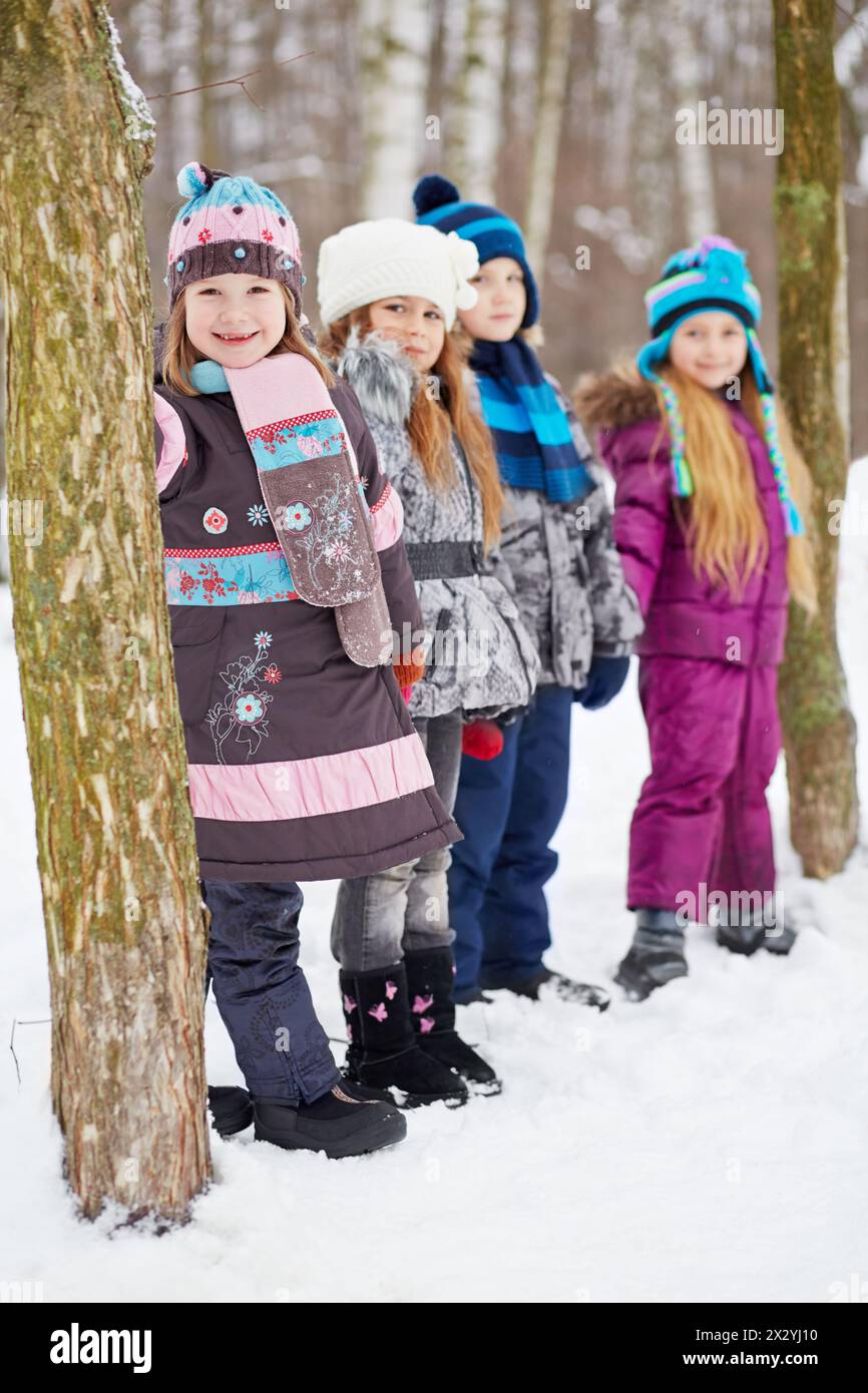 Three girls and one boy stand in winter park between two trees, focus ...