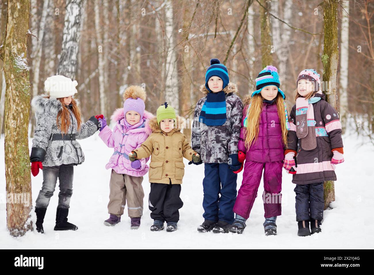 Six children stand holding hands in winter park, four older and two ...