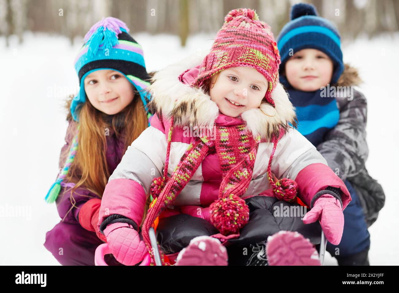 Older girl and boy push sled in which younger girl sits,focus on first ...