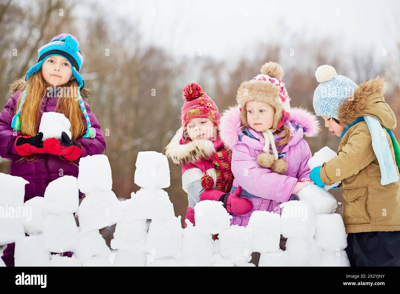 Girl with three little children build wall from snow bricks Stock Photo ...
