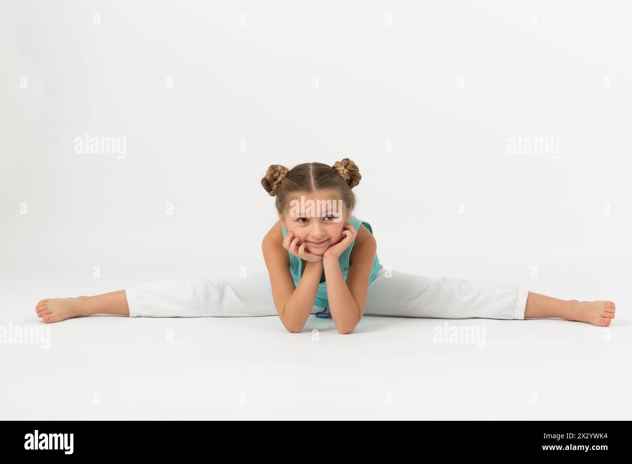 A girl makes gymnastic exercise sitting on splits propped head in hands ...