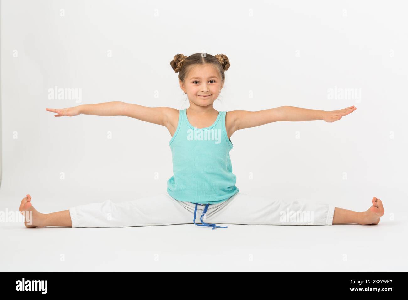 A girl makes gymnastic exercise sitting on splits and making hands in ...