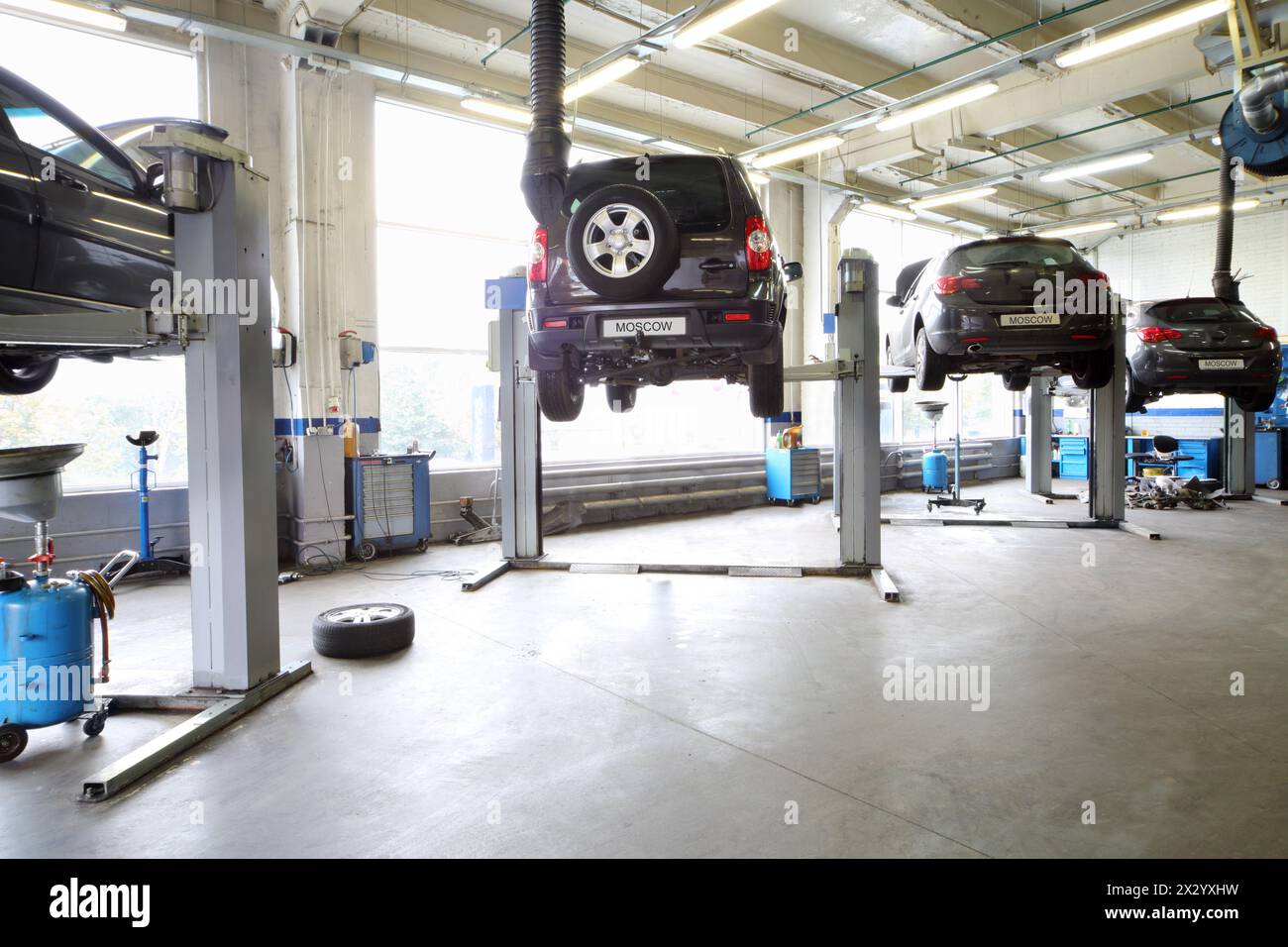 Four black cars on lifts in small service station. Cars prepared to ...