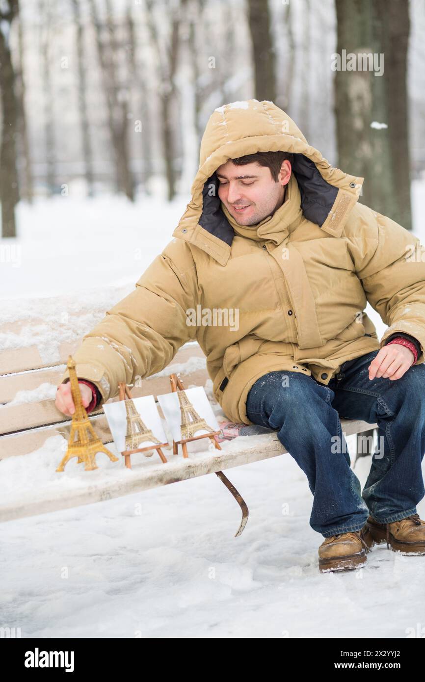 A man sits on a bench in the park with a small figures Eiffel Tower ...