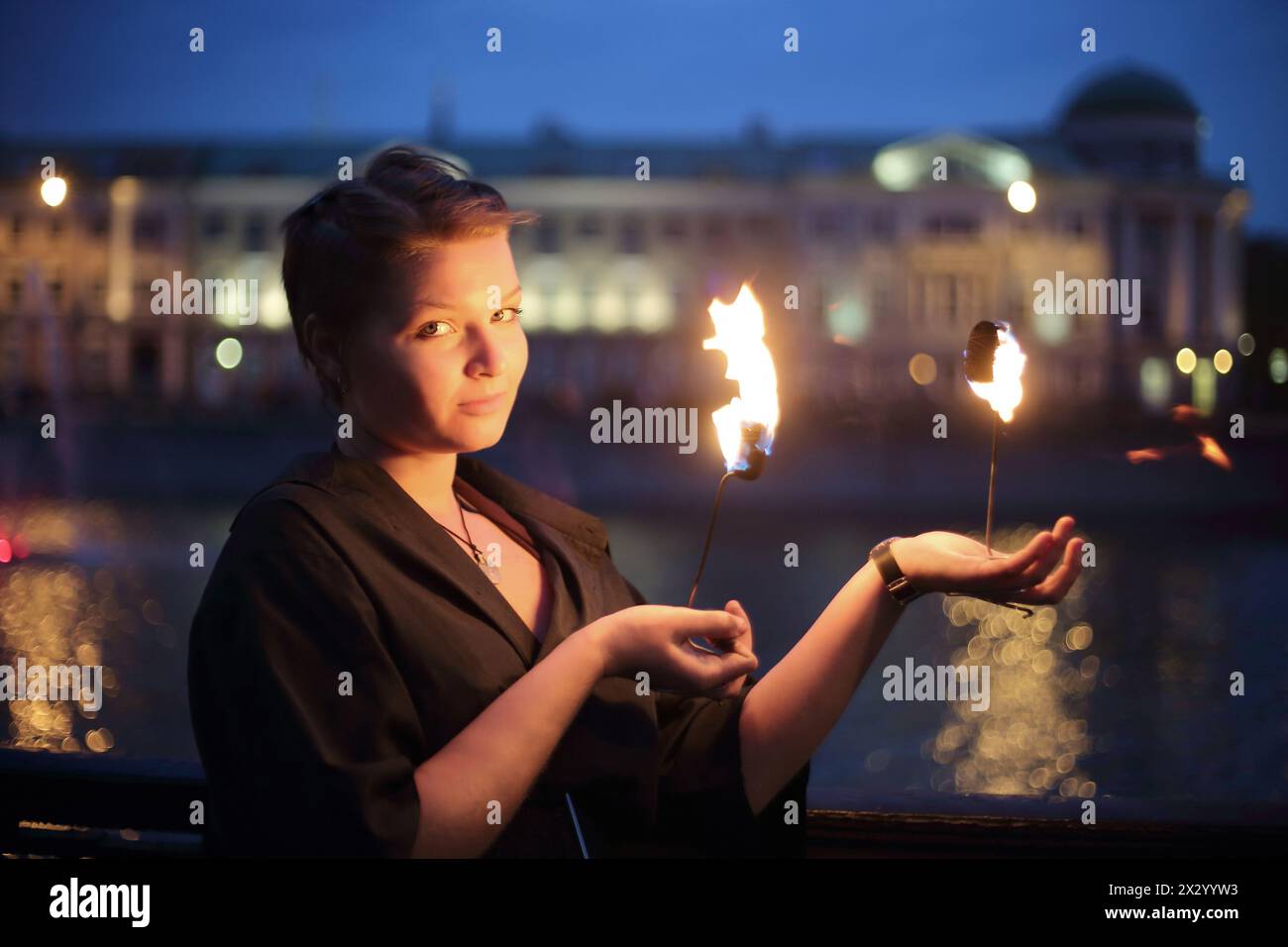A girl in a black dress shows a fire show in the night near the river ...