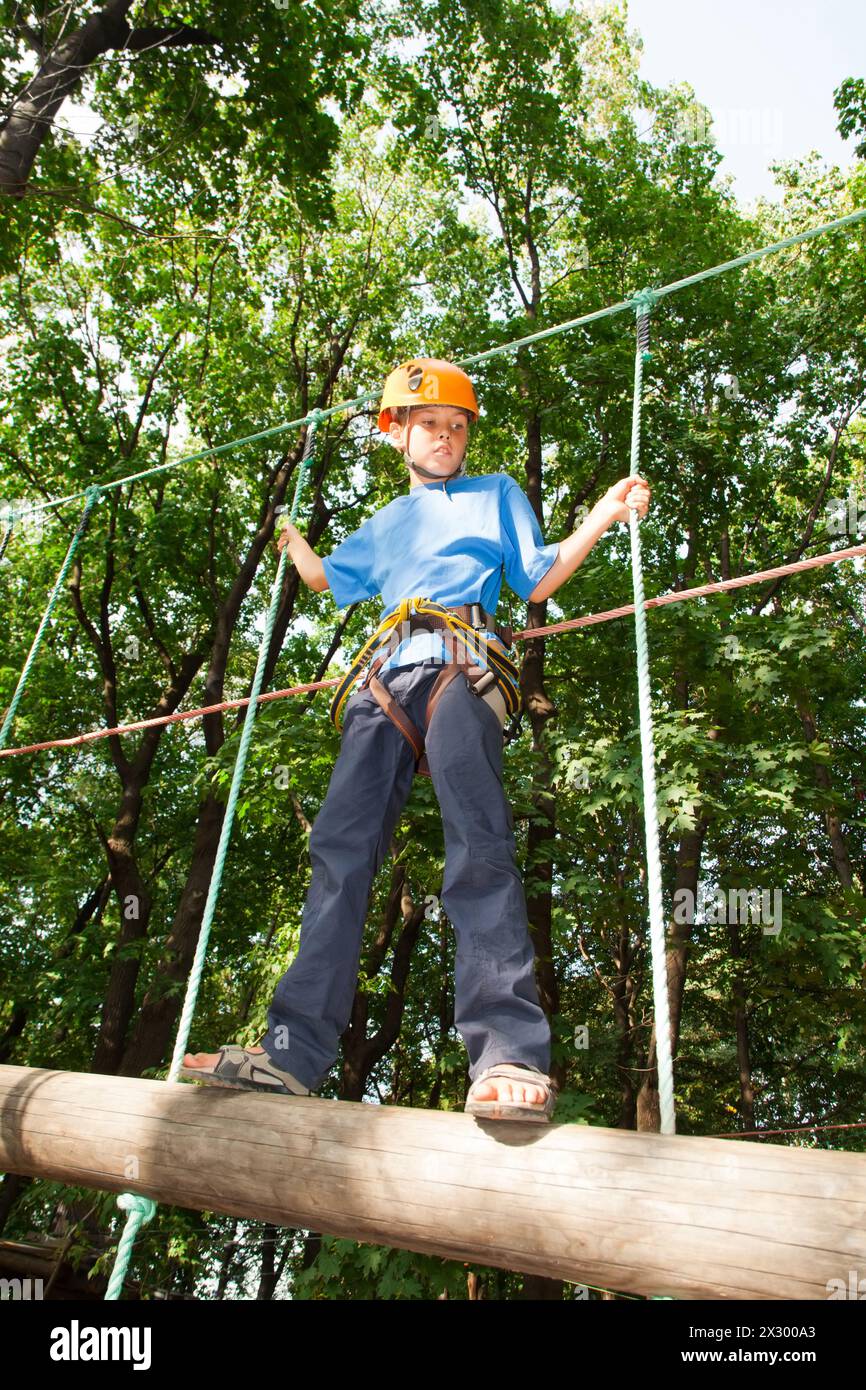 Young guy with equipment climber moves on a balk holding the ropes ...