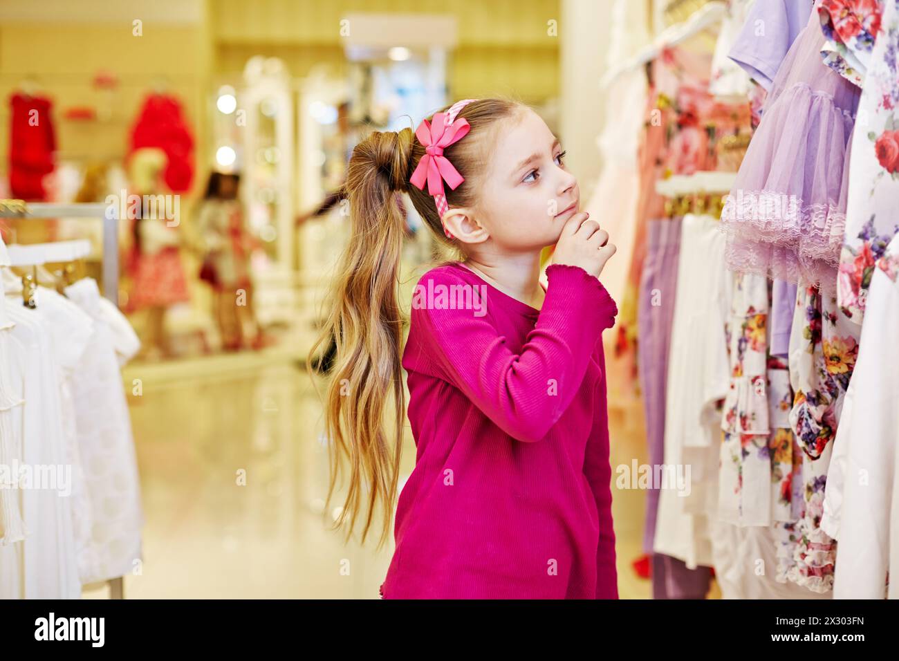 Little girl looks with interest, touching chin with fingers, upon ...