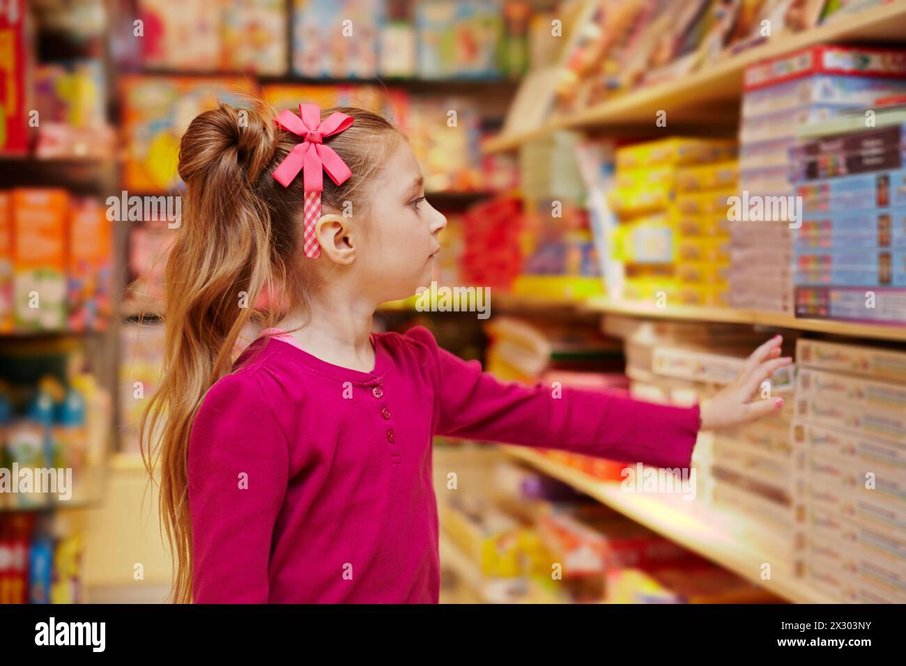 Little girl stretches to shelf with table games in book department of ...