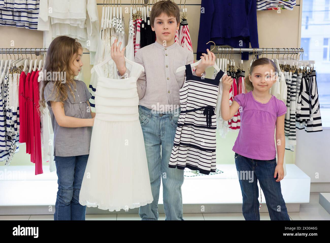 The boy helps cute girls to choose dress in shop of childrens clothing ...