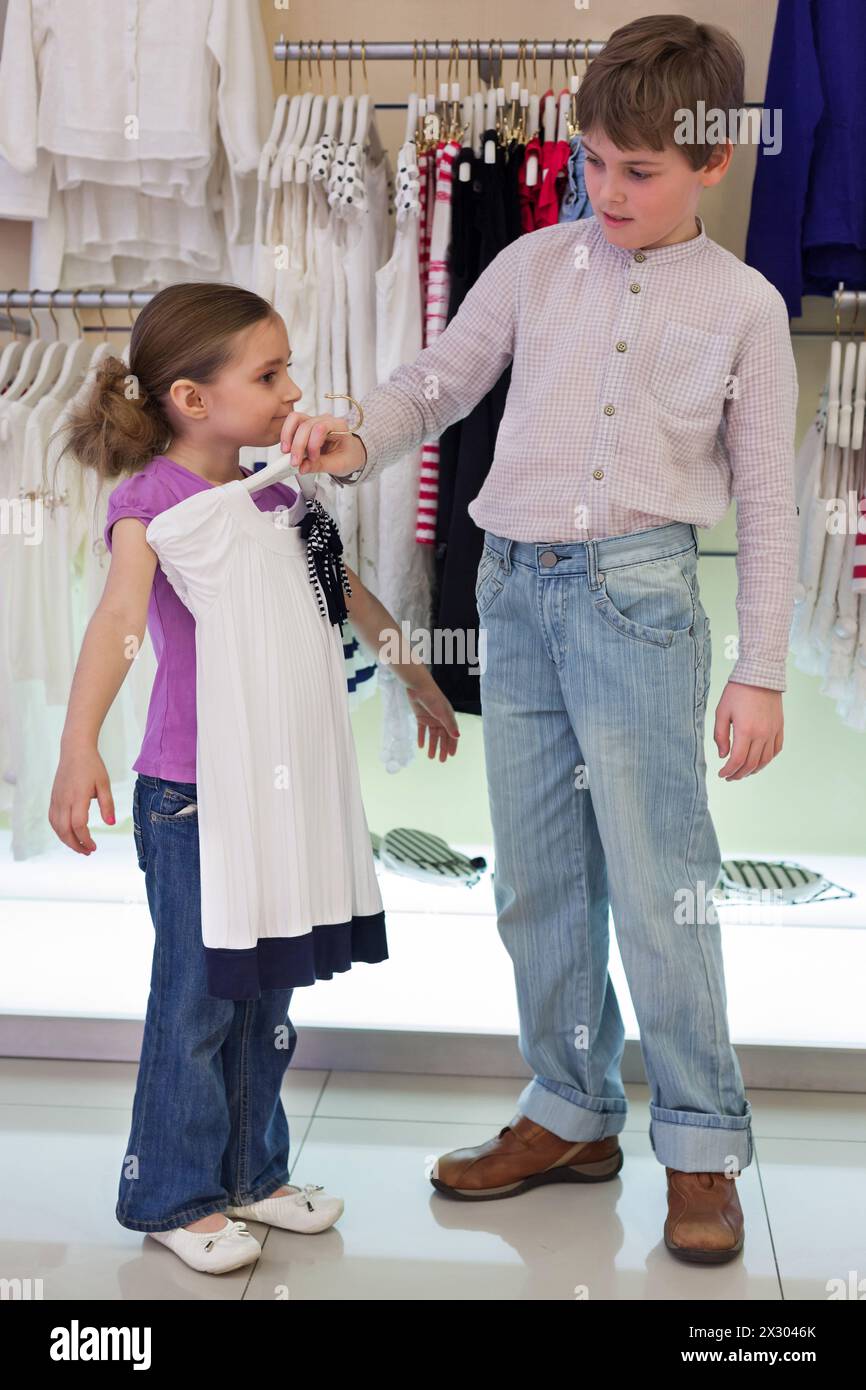 The boy helps sister to choose clothes in shop of childrens clothing ...