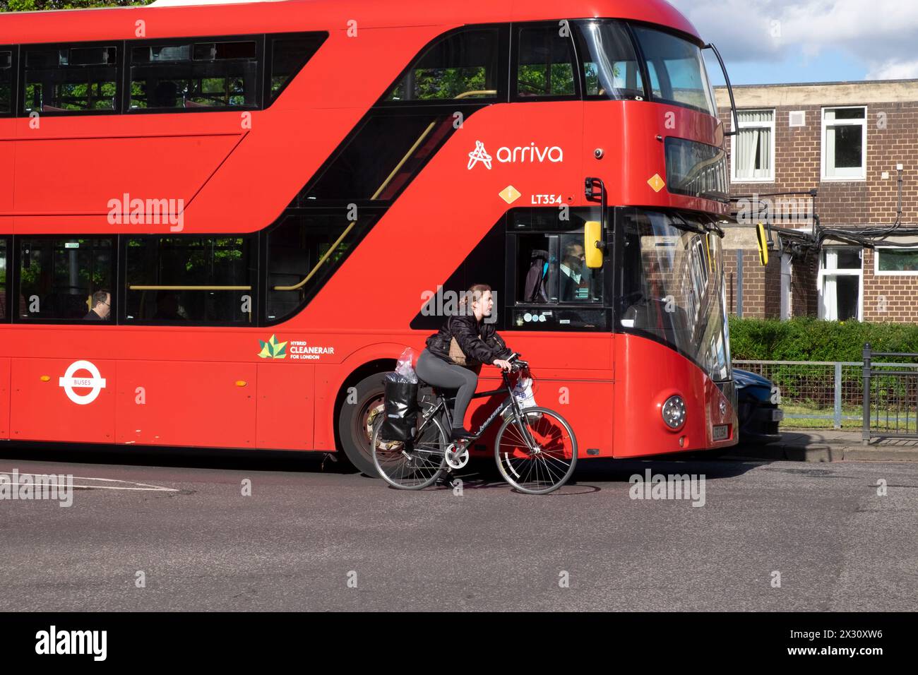 Female young woman cyclist on bike riding bicycle next to red Arriva double decker bus in ...