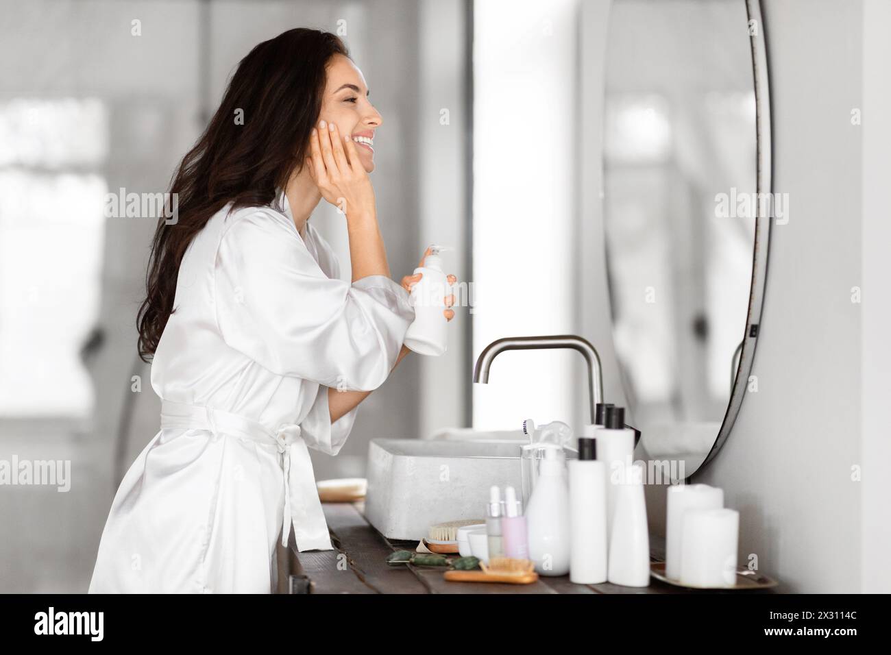 Woman applying skincare in a robe, side view Stock Photo - Alamy